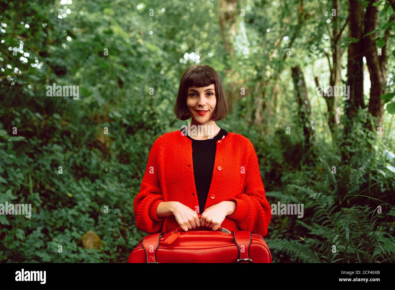 Woman in red with big red suitcase in forest Stock Photo - Alamy