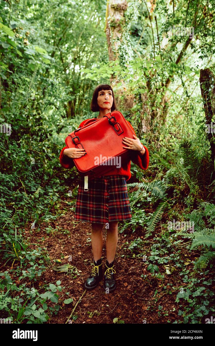 Woman in red with big red suitcase in forest Stock Photo - Alamy