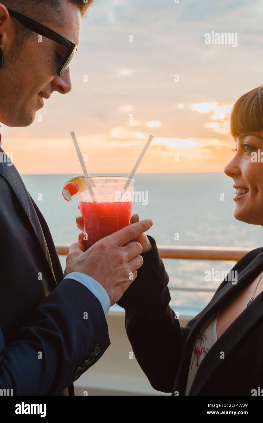 Side view of young attractive couple drinking red beverage with straws ...