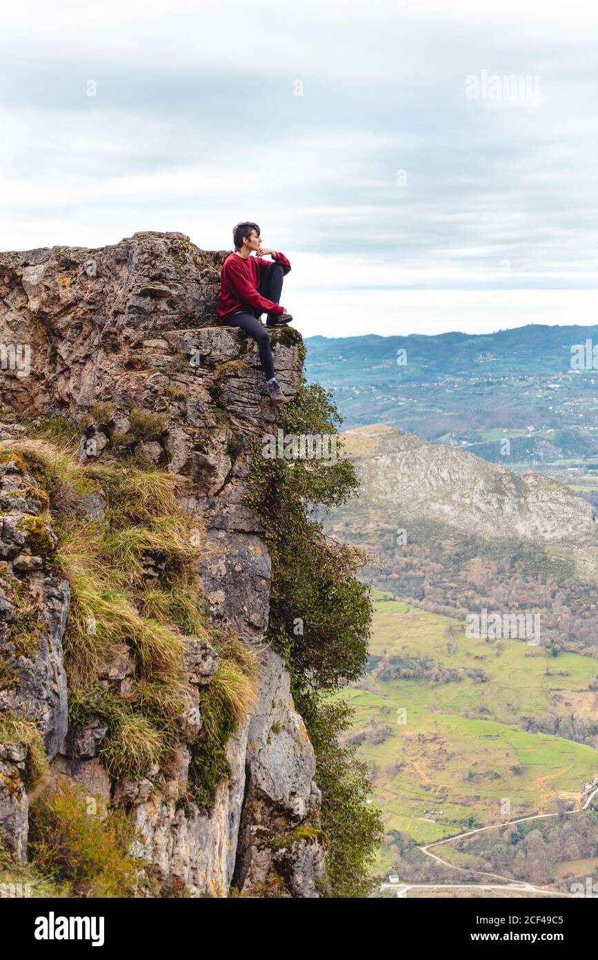Side view of tourist sitting on edge of cliff enjoying freedom and ...