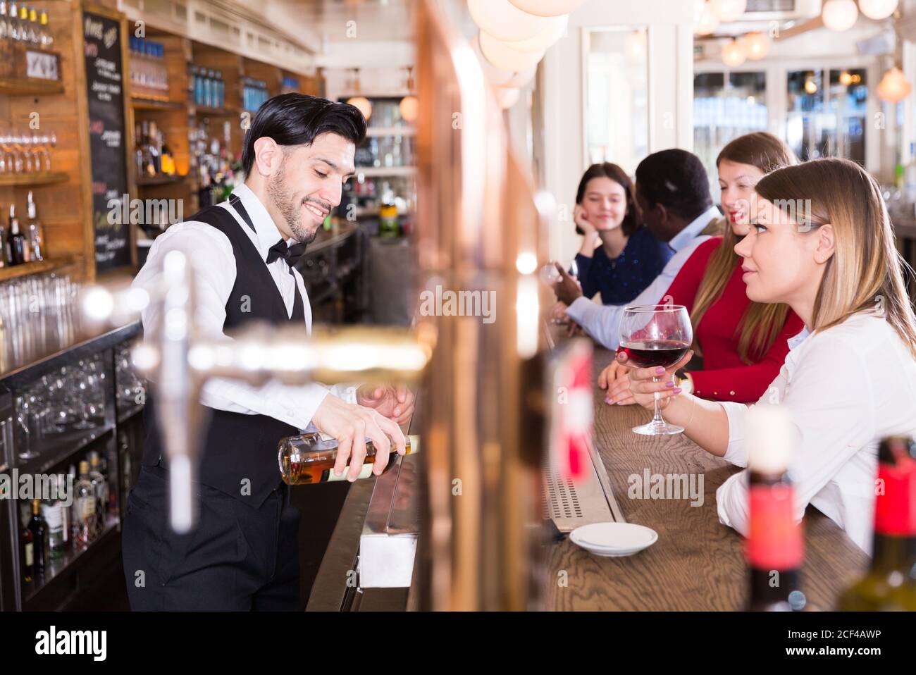 Barman is servicing young people who are drinking alcohol in bar in ...