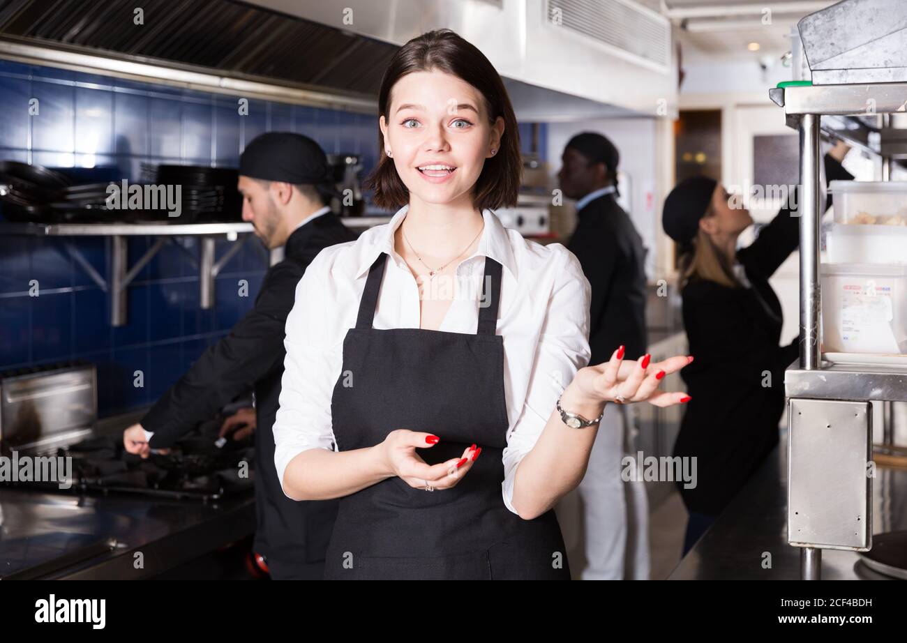 Cheerful young waitress showing modern kitchen of restaurant with ...