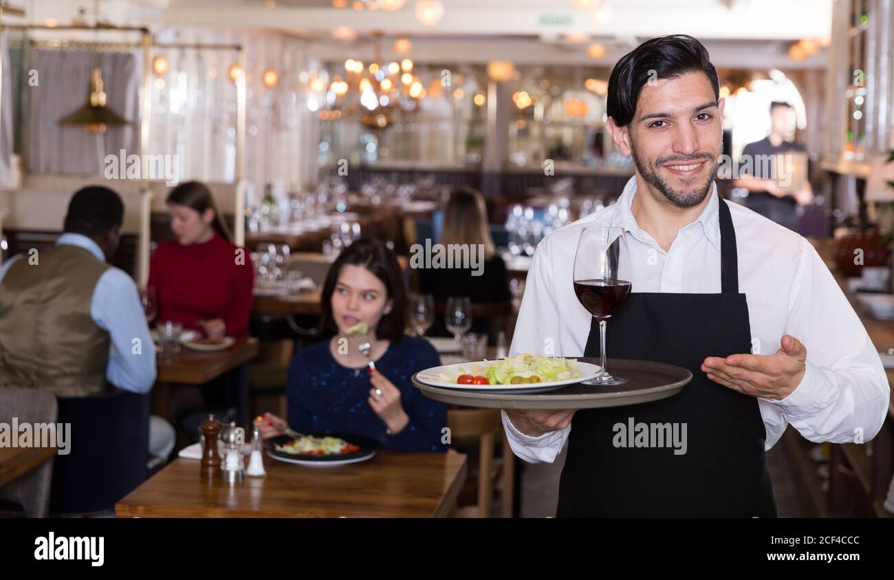 Portrait of smiling waiter with serving tray meeting restaurant guests ...