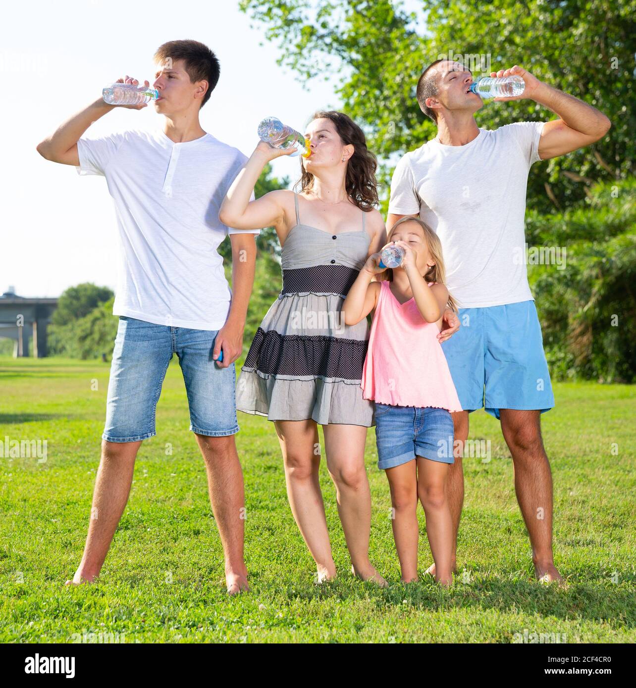 Parents with teenager son and daughter drinking cold water from plastic ...