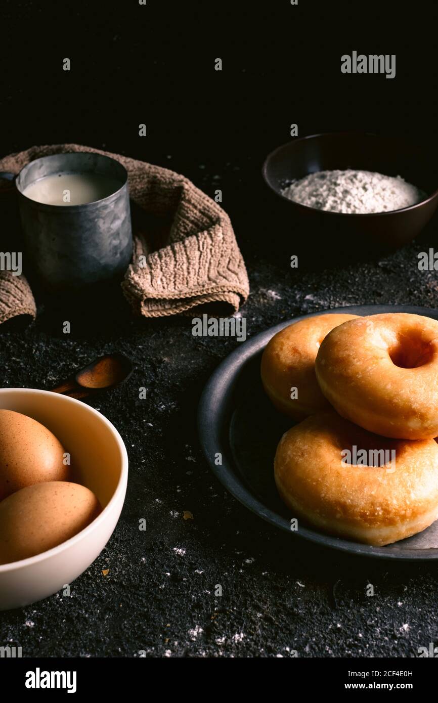 Fresh doughnuts placed on rough table near various pastry ingredients ...