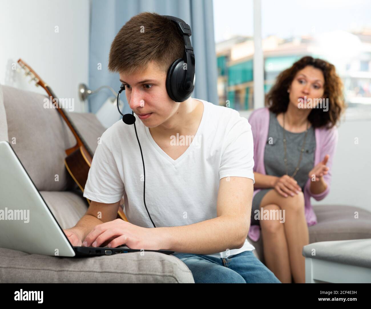 Teenage boy absorbedly playing on laptop at home on background of his ...