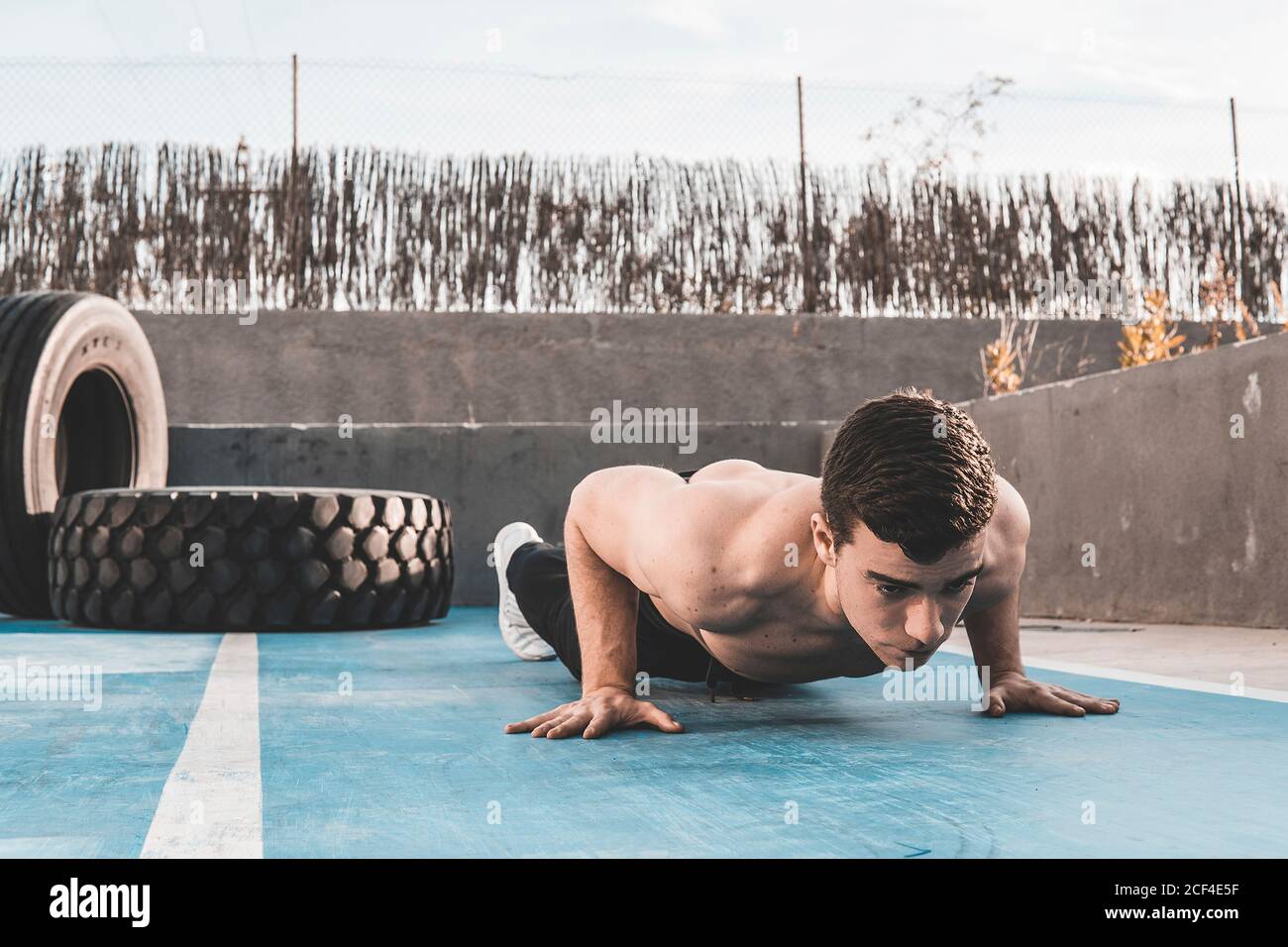 Muscular young guy doing push ups while exercising on concrete floor of ...