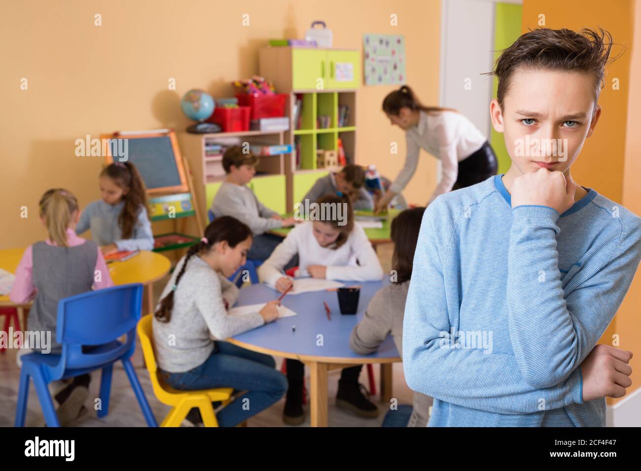 Portrait of upset boy in schoolroom on background with pupils studying ...