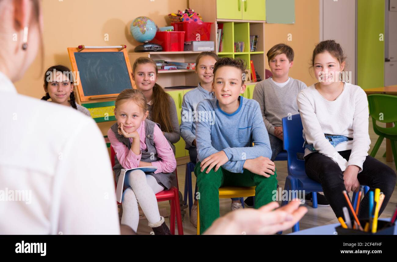 Glad boys and girls listening teacher, sitting at lesson in classroom ...