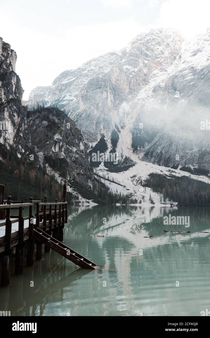 Wooden bridge pier on stilts on nebulous lake with reflection of ...