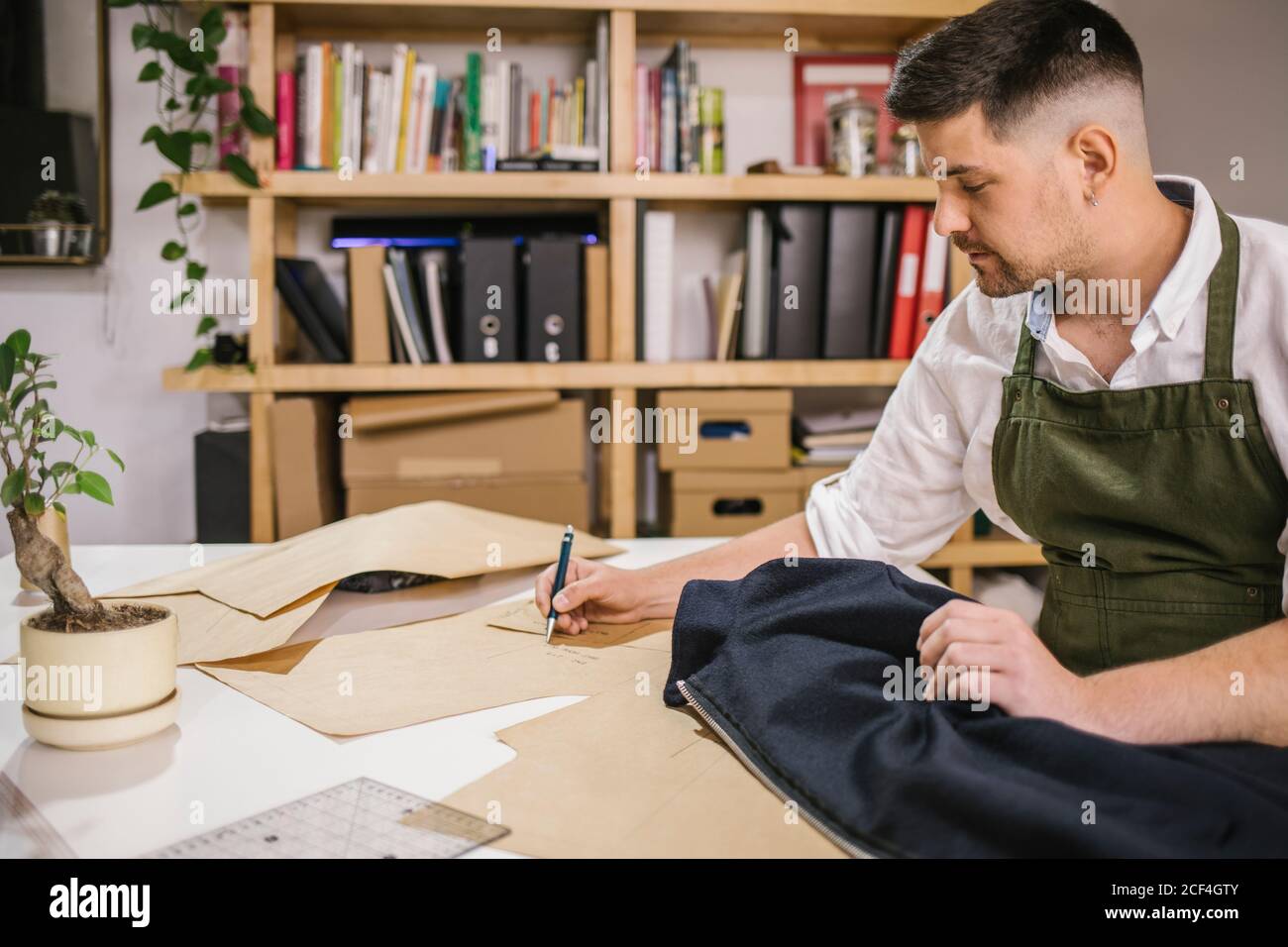 Crop young male dressmaker writing with pen on sewing pattern examining ...