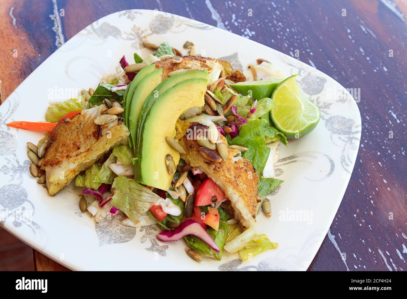 Grilled snapper on a bed of llettuce salad with avocado slices and ...