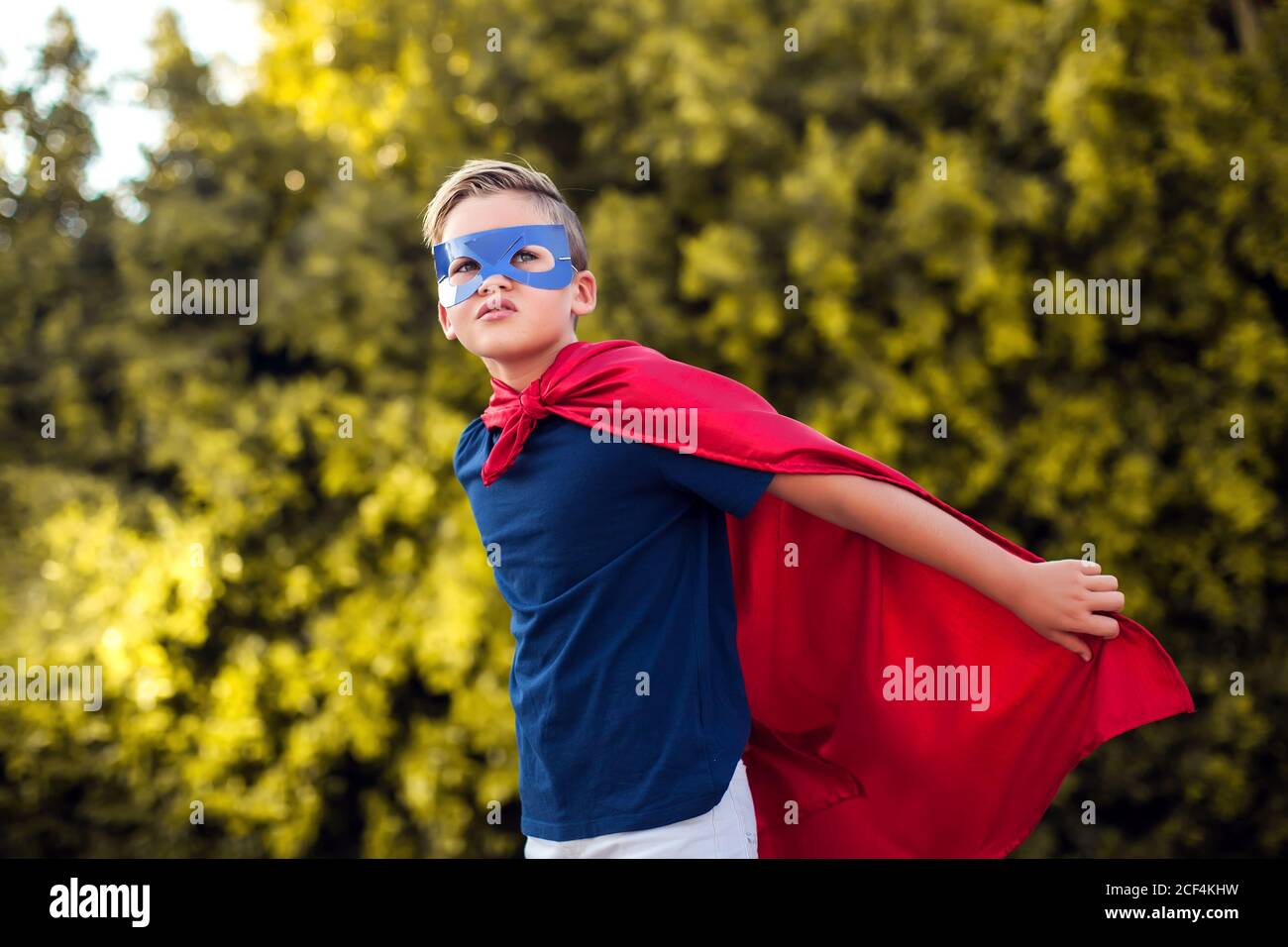 Superhero kid boy against green background outdoor. Childhood, success ...