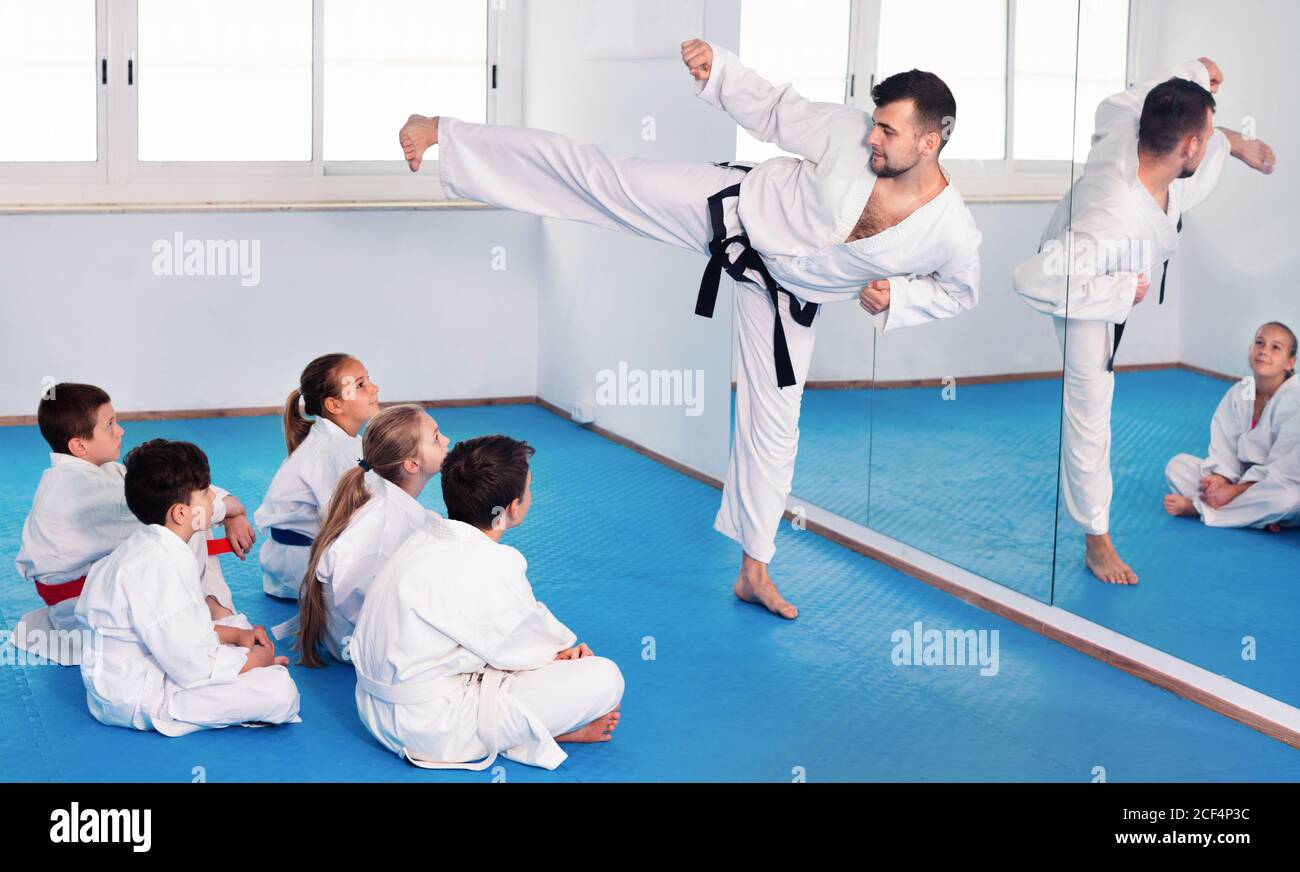 Smiling positive coach showing new martial moves to children in karate ...