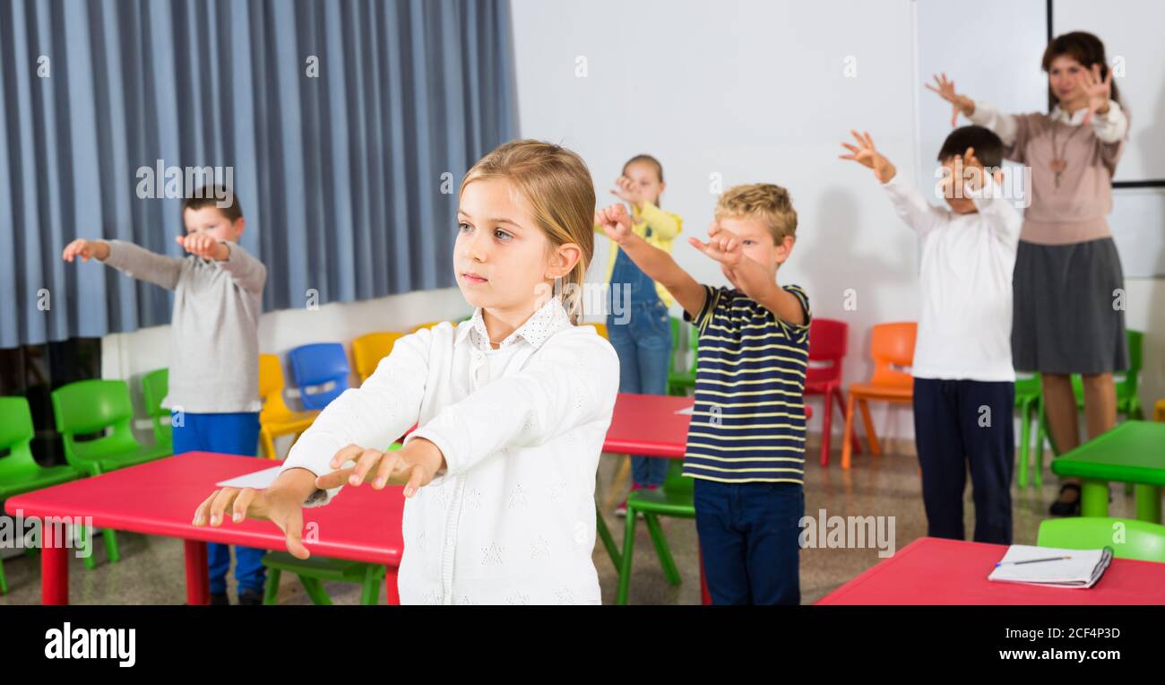 Portrait of children stretching with friendly female teacher during ...