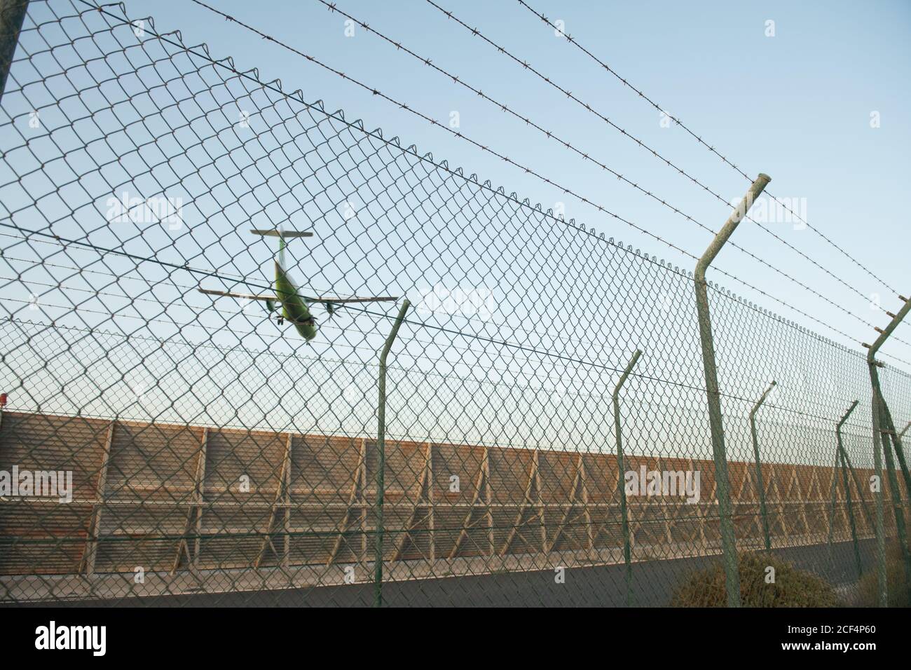 Modern aircraft flying against cloudless blue sky behind security fence ...