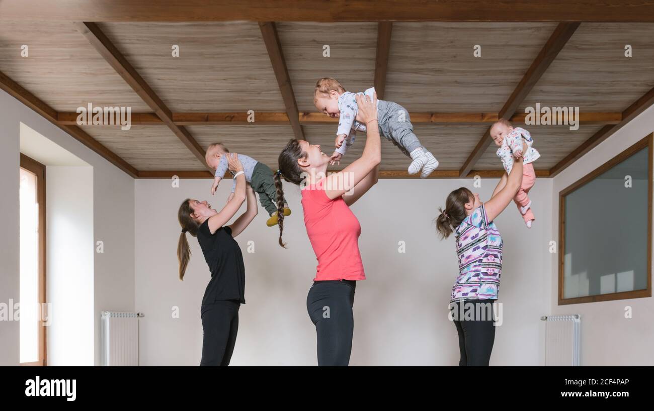Side view of women in sportswear lifting cute babies over heads while ...