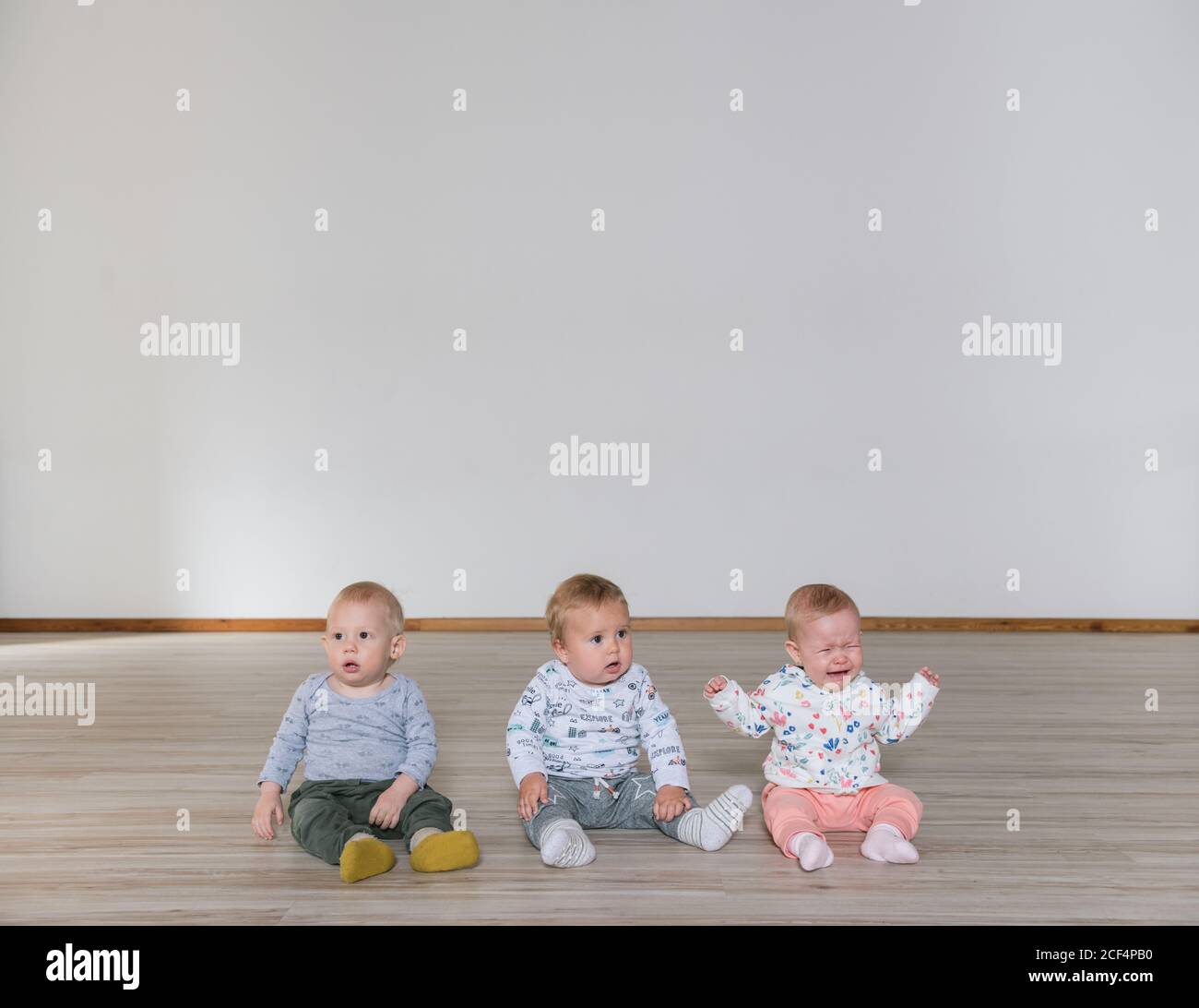 Three adorable babies crying and looking around while sitting on floor ...