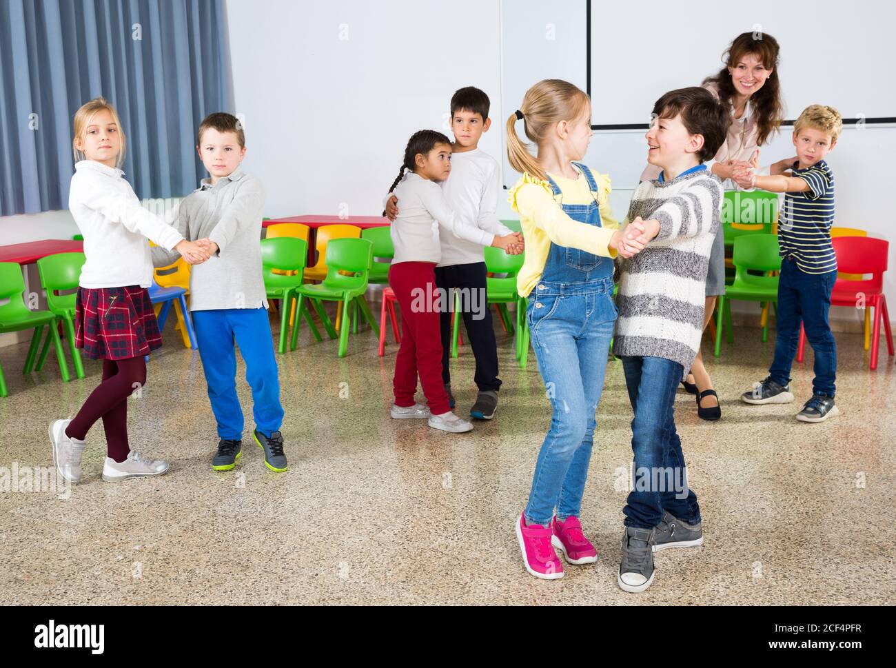 Group of cheerful school kids learning to dance in pairs with their ...