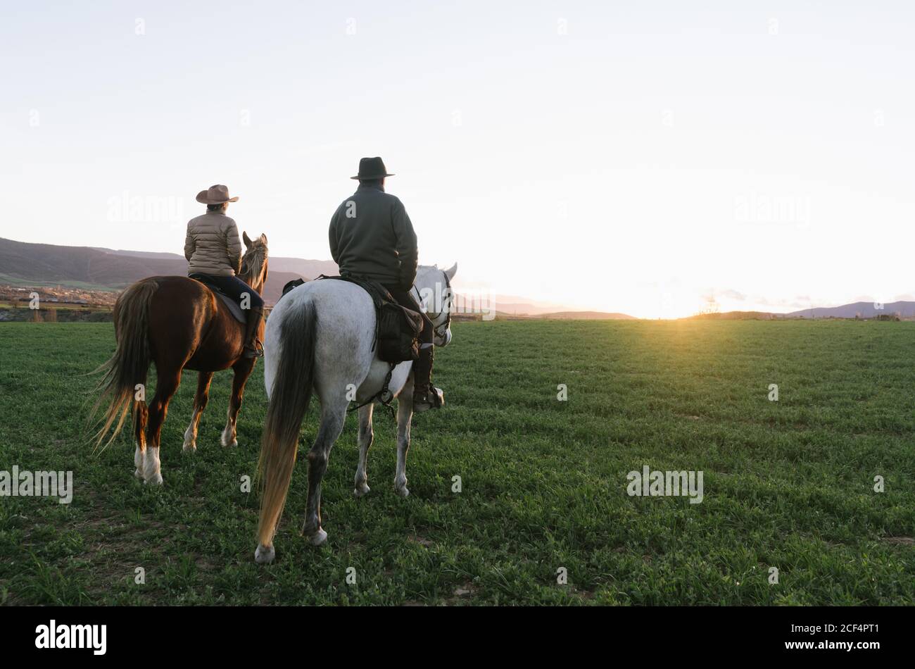 Back view of man and Woman riding horses against sunset sky on ranch ...