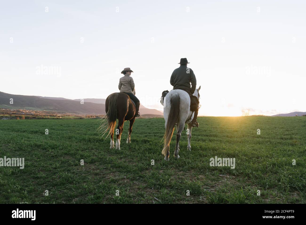 Back view of man and Woman riding horses against sunset sky on ranch ...