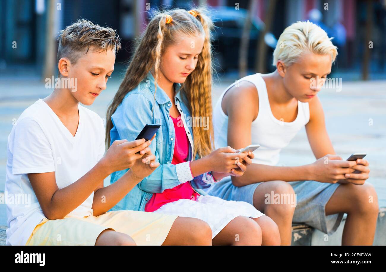 Three glad cheerful smiling children keened on mobile phones during ...