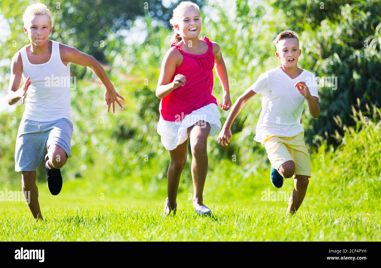 Smiling kids playing active games in summer park chasing each other ...