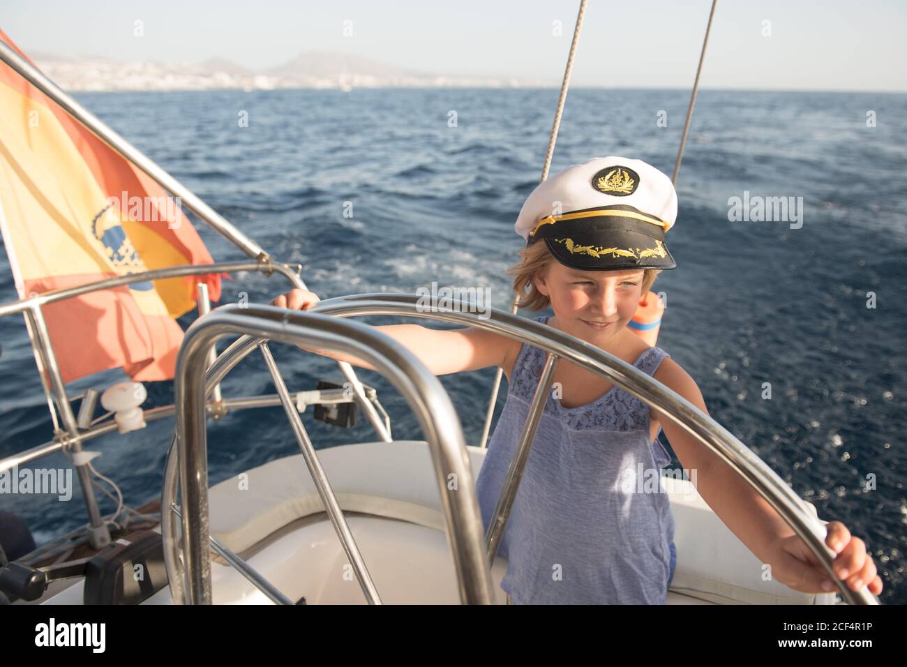 Positive kid in captain hat floating on expensive boat on sea in sunny ...