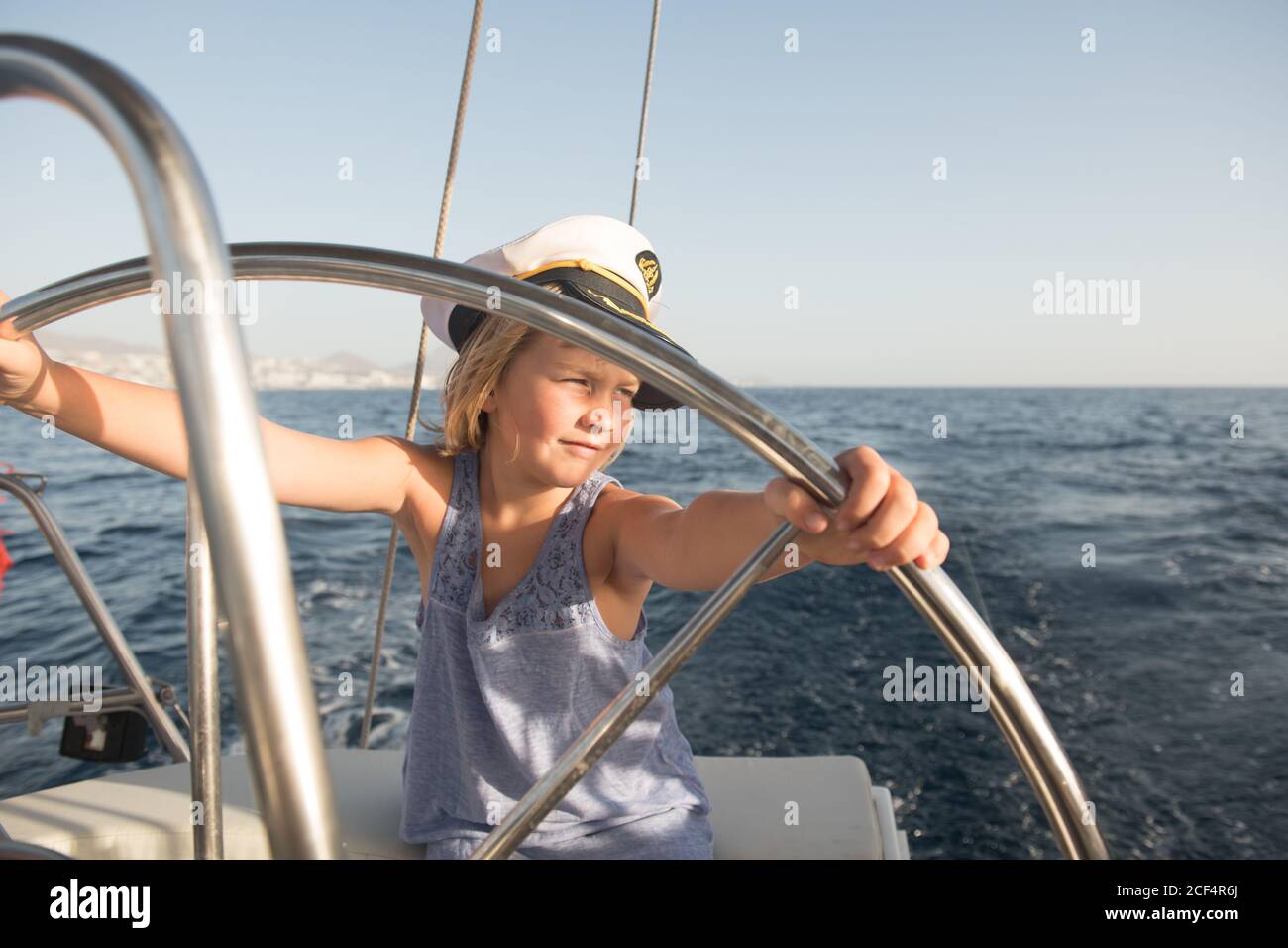 Positive kid in captain hat floating on expensive boat on sea in sunny ...