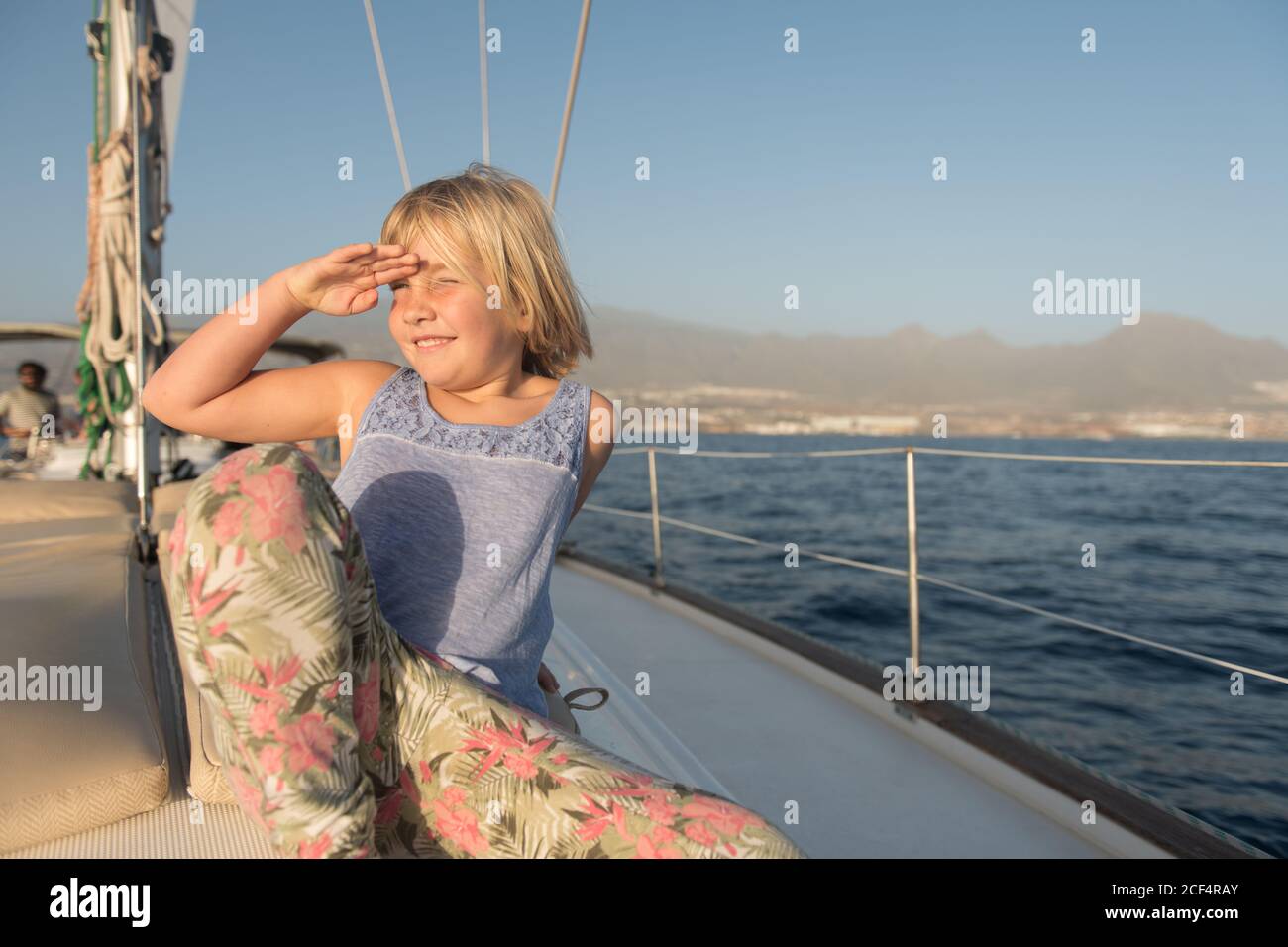 Positive kid with hand near face peeping from sun and sitting on side ...
