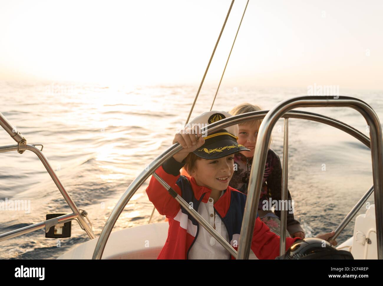 Positive kids in captain hat floating on expensive boat on sea in sunny ...