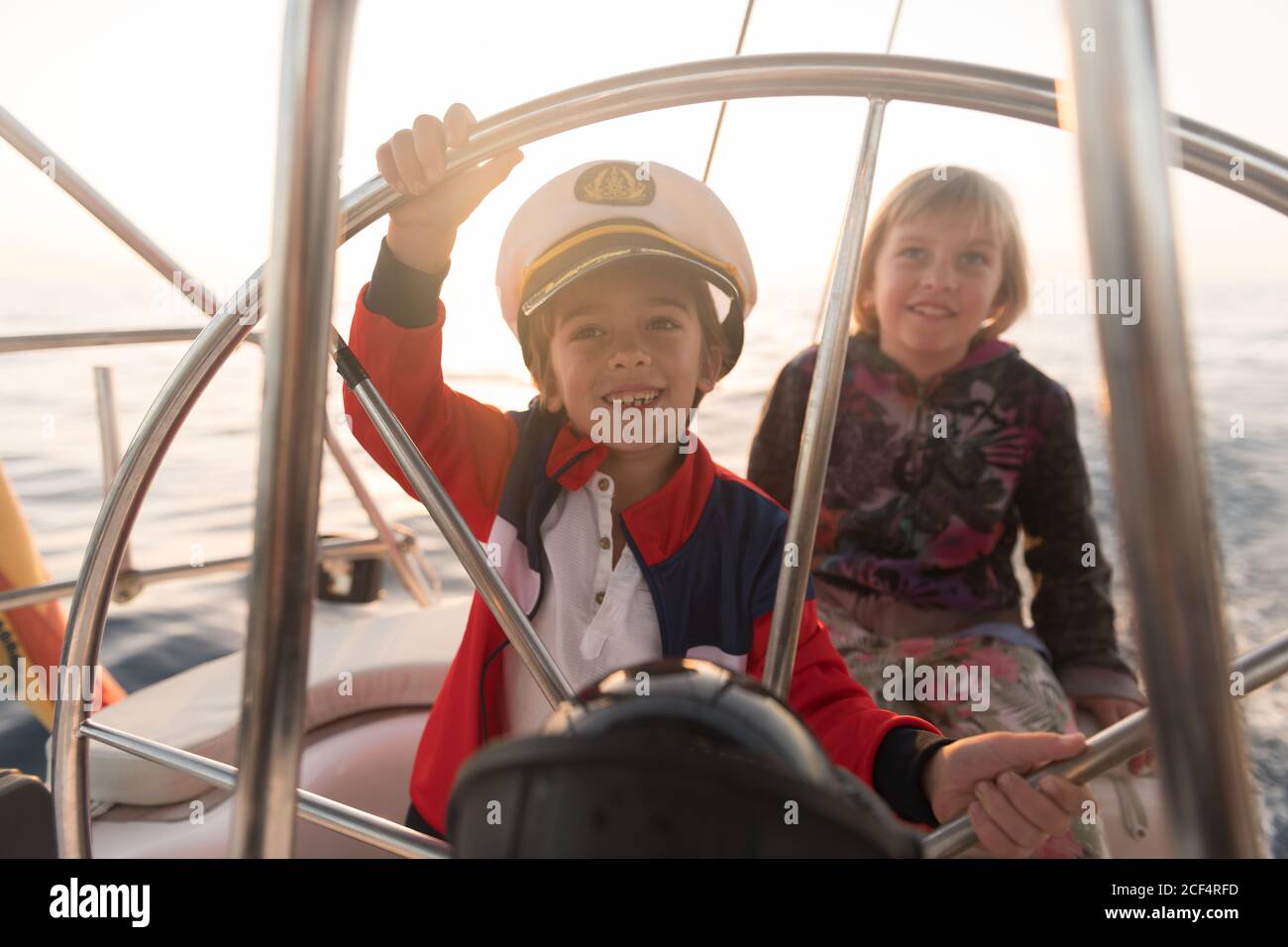 Positive kids in captain hat floating on expensive boat on sea in sunny ...