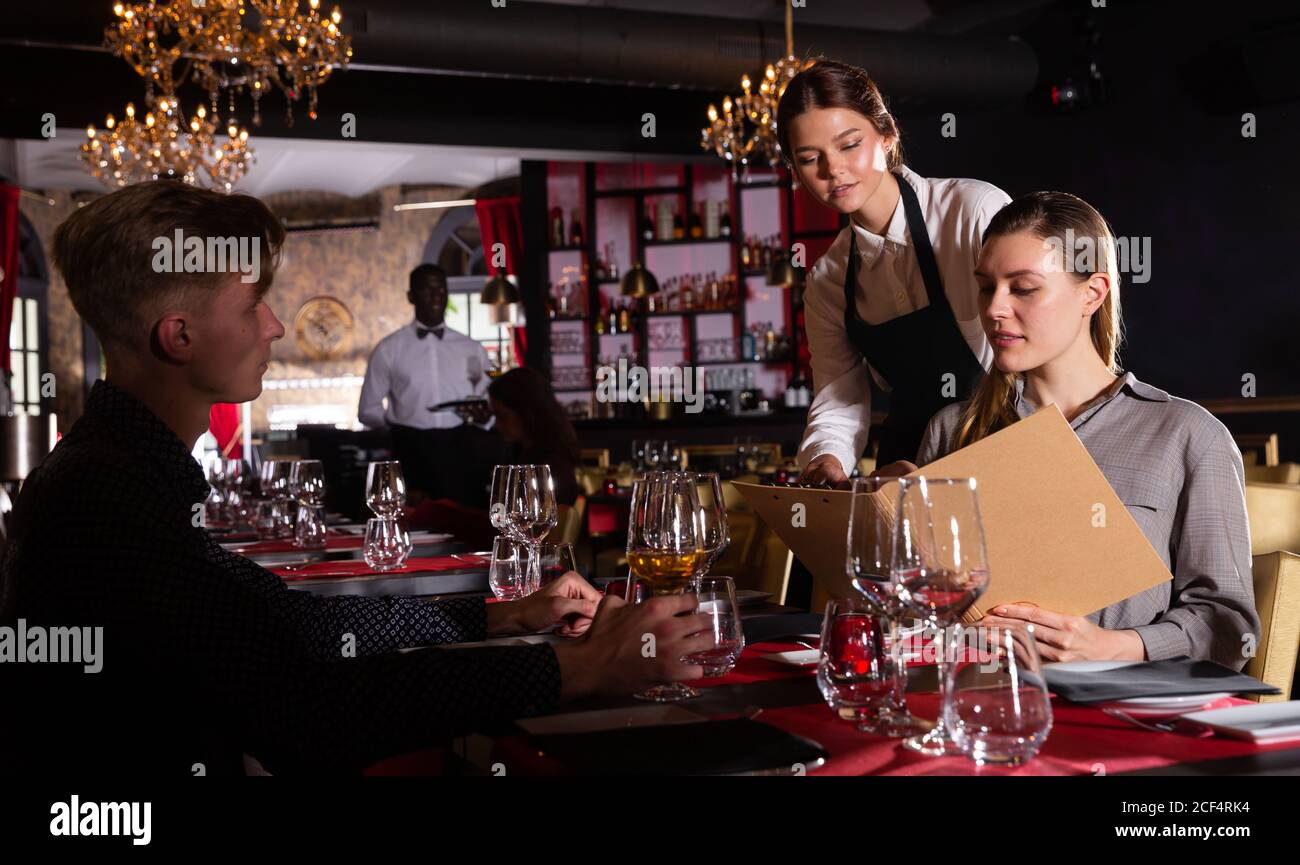 Friendly smiling female waiter bringing order to visitors in luxurious ...