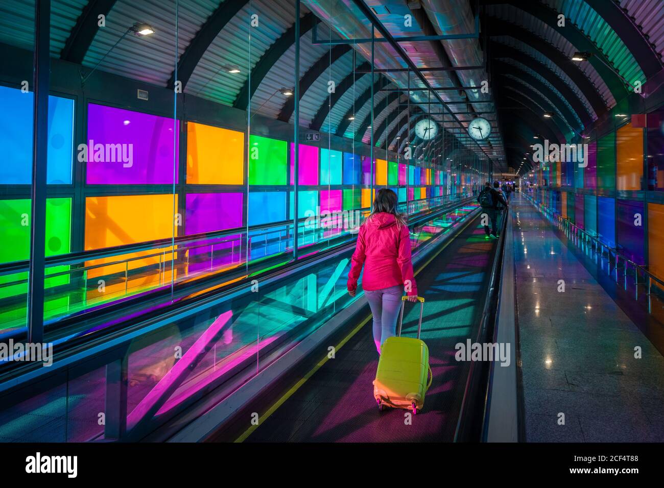 anonymous female with suitcase riding mowing walkway near colorful ...