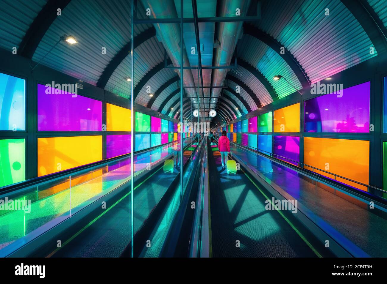 anonymous female with suitcase riding mowing walkway near colorful ...