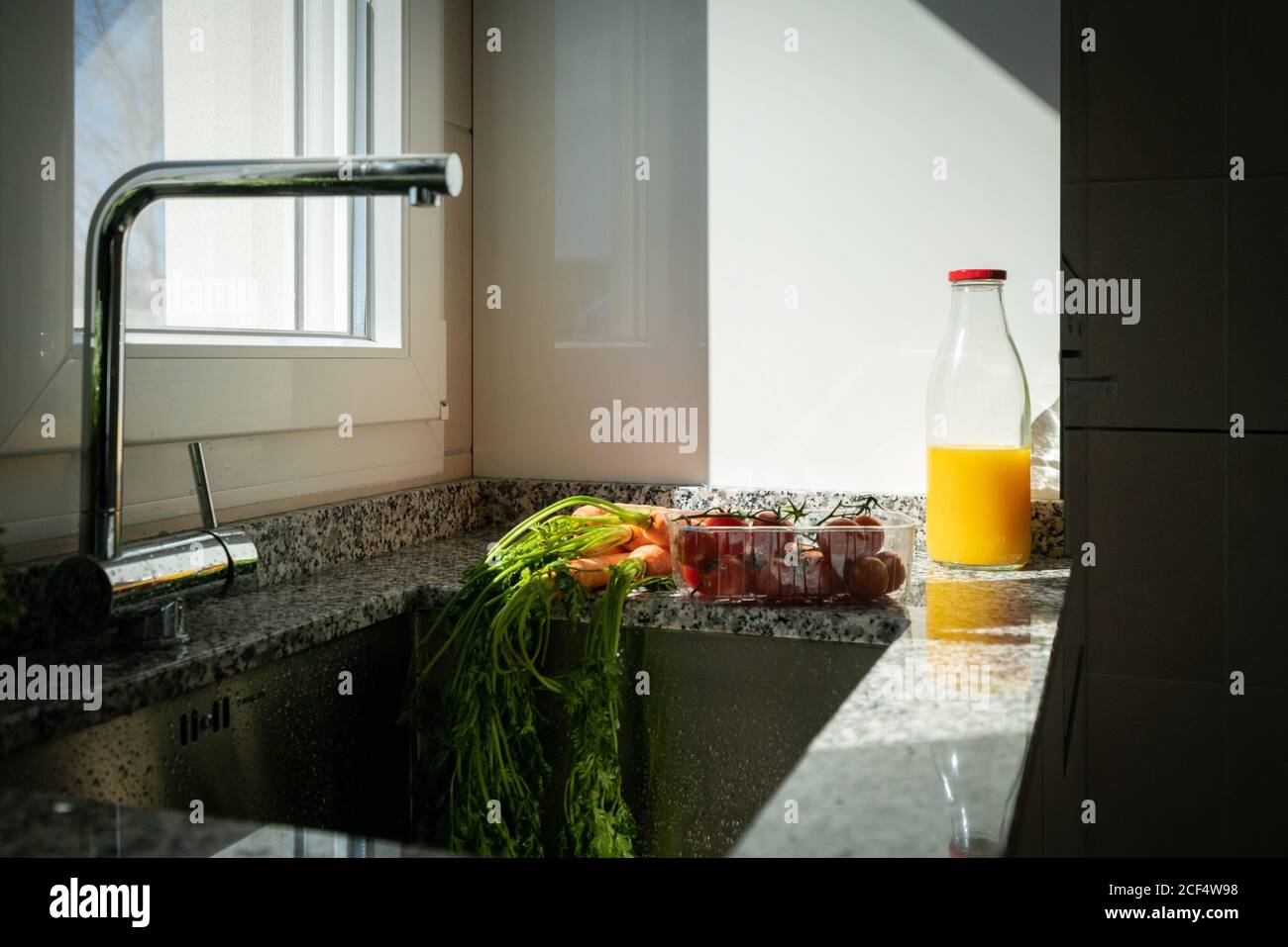 Vegetables and bottle of orange juice near a kitchen sink at home Stock ...