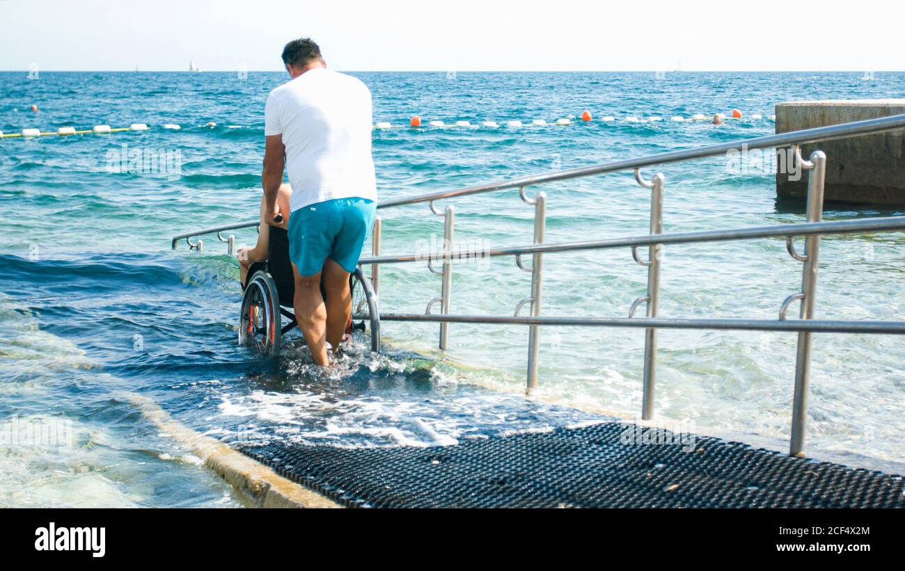 Disabled man at beach swimming on a wheelchair with assistance help on ...