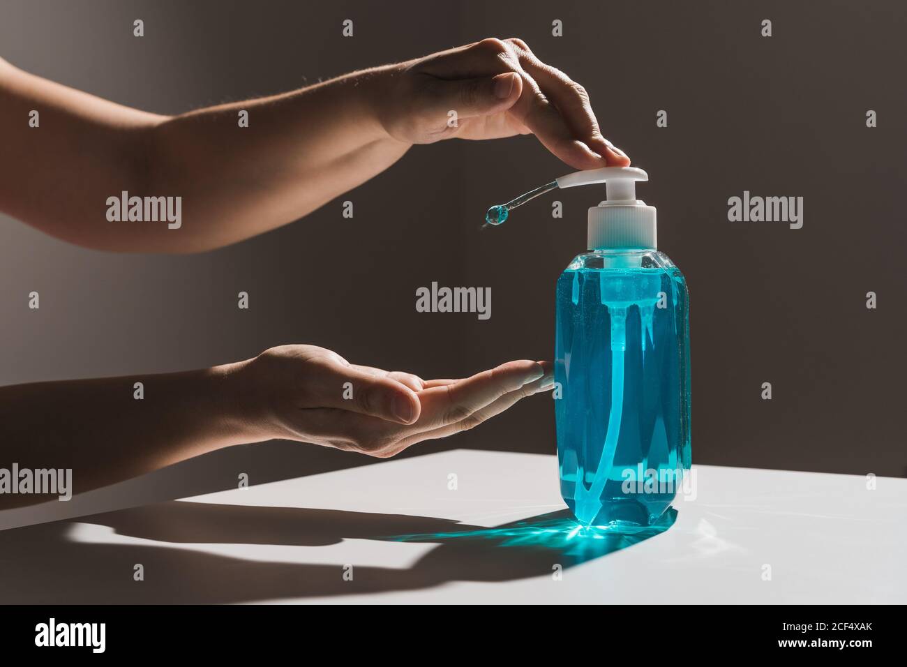 Crop faceless person pulling hands for plastic blue liquid soap bottle ...
