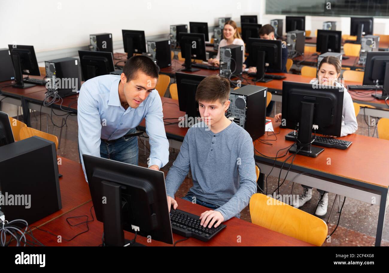 Teacher explains to male student how to use program on the computer ...