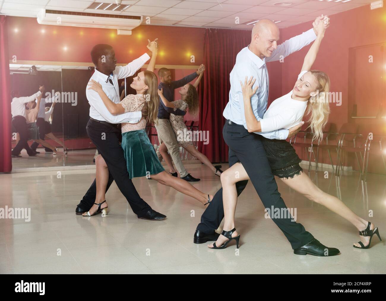 Portrait of positive adult pairs enjoying tango in modern dance hall ...