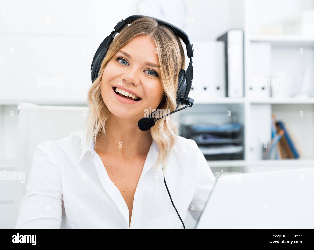 Young call center employee in headphones is sitting near laptop in the ...