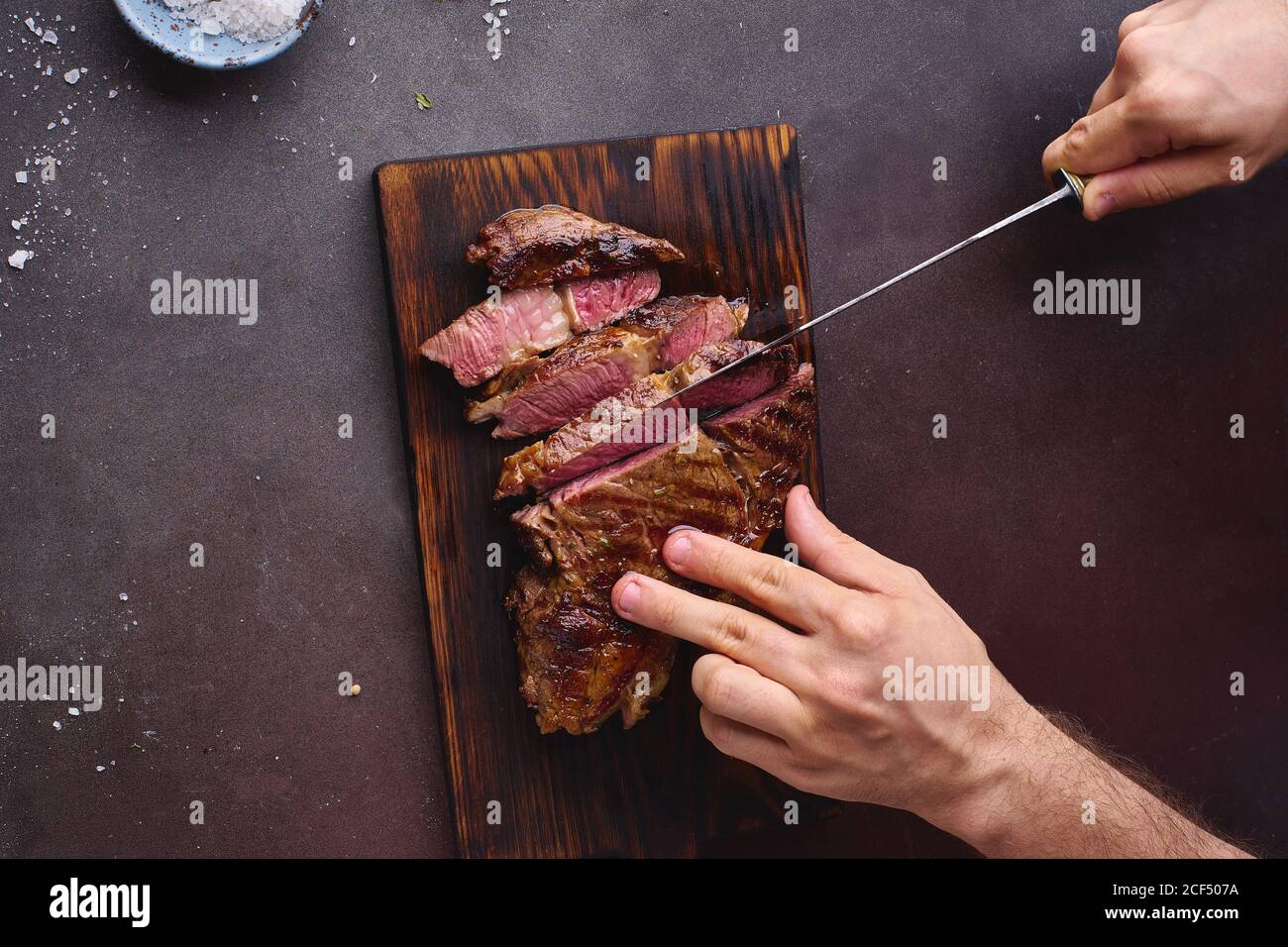 Male hands cutting cooked until medium ribeye steak on wooden cutting ...