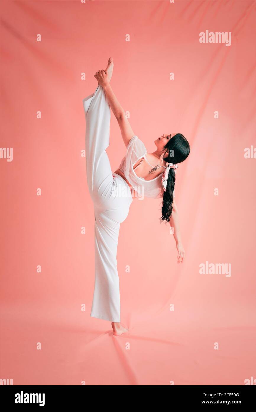 Back view of slim female in white outfit doing splits while dancing ...