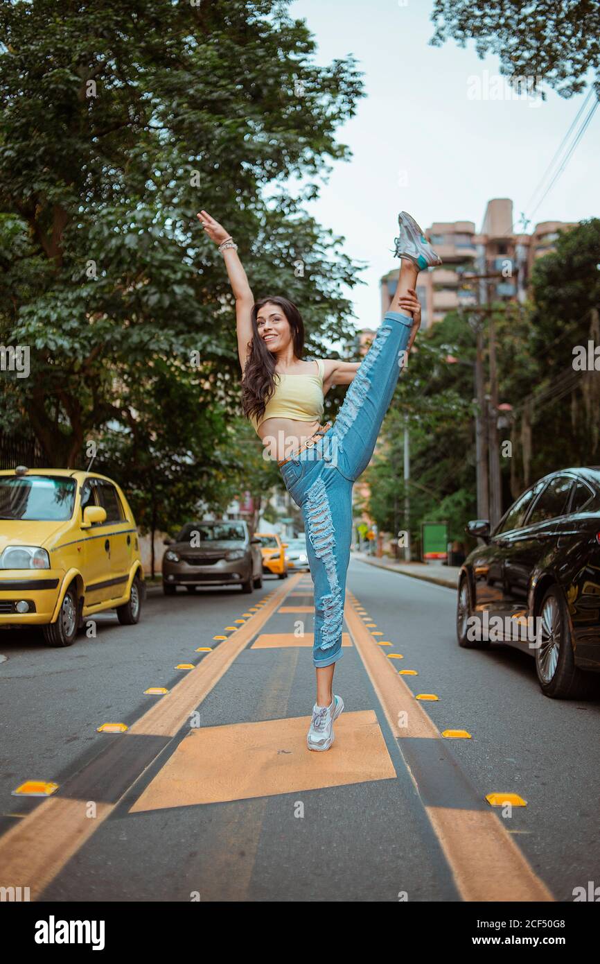 Full body cheerful female in casual clothes doing splits with raised ...