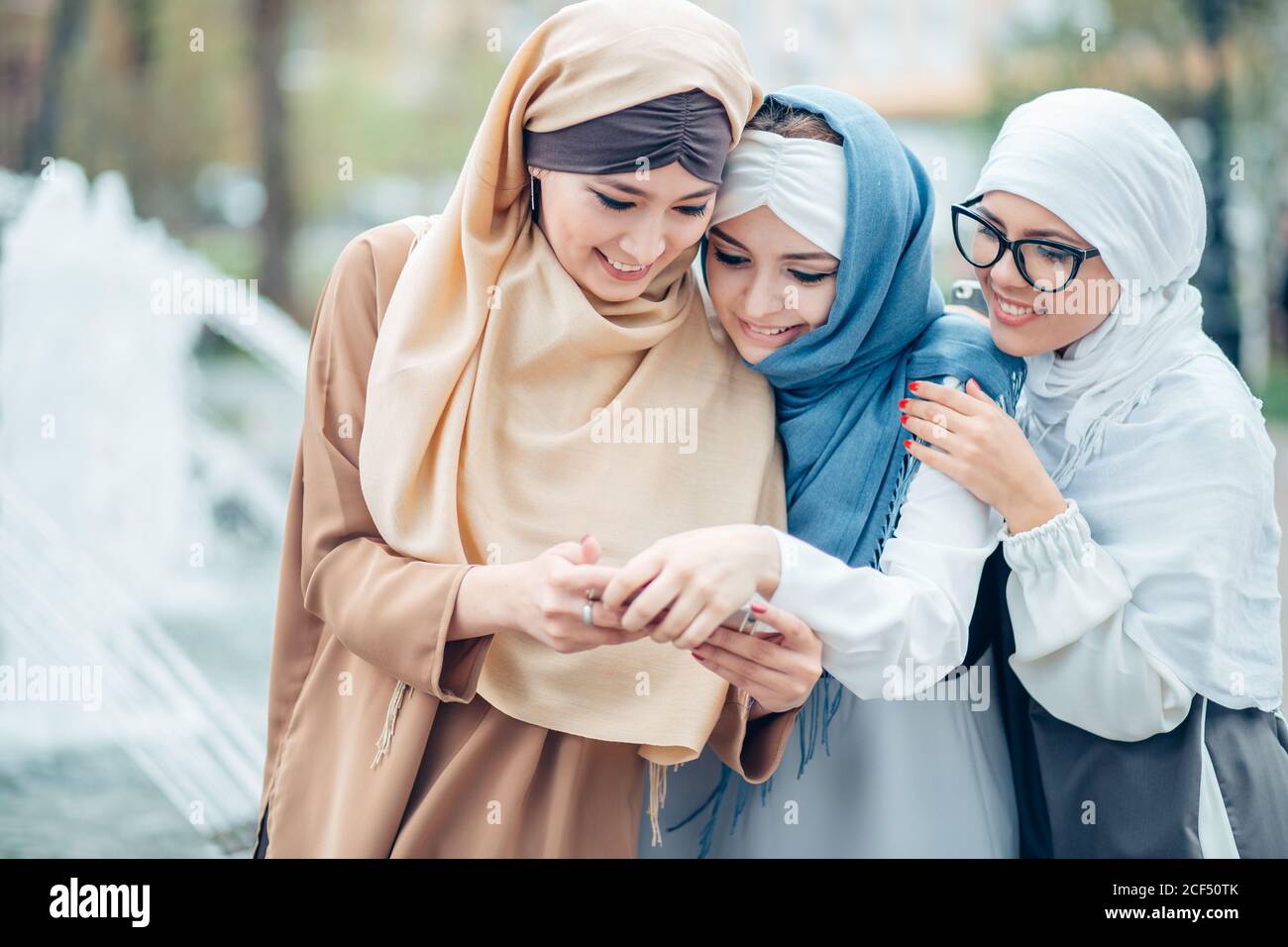 A picture of three muslim girl friends using smartphone. on the ...