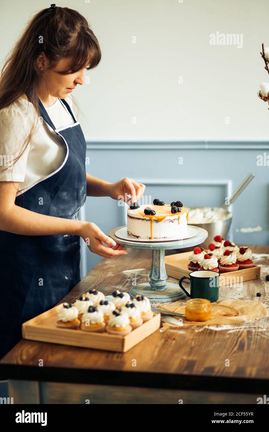 Pastry chef in the kitchen decorating a cake of chocolate,fruit,candies ...