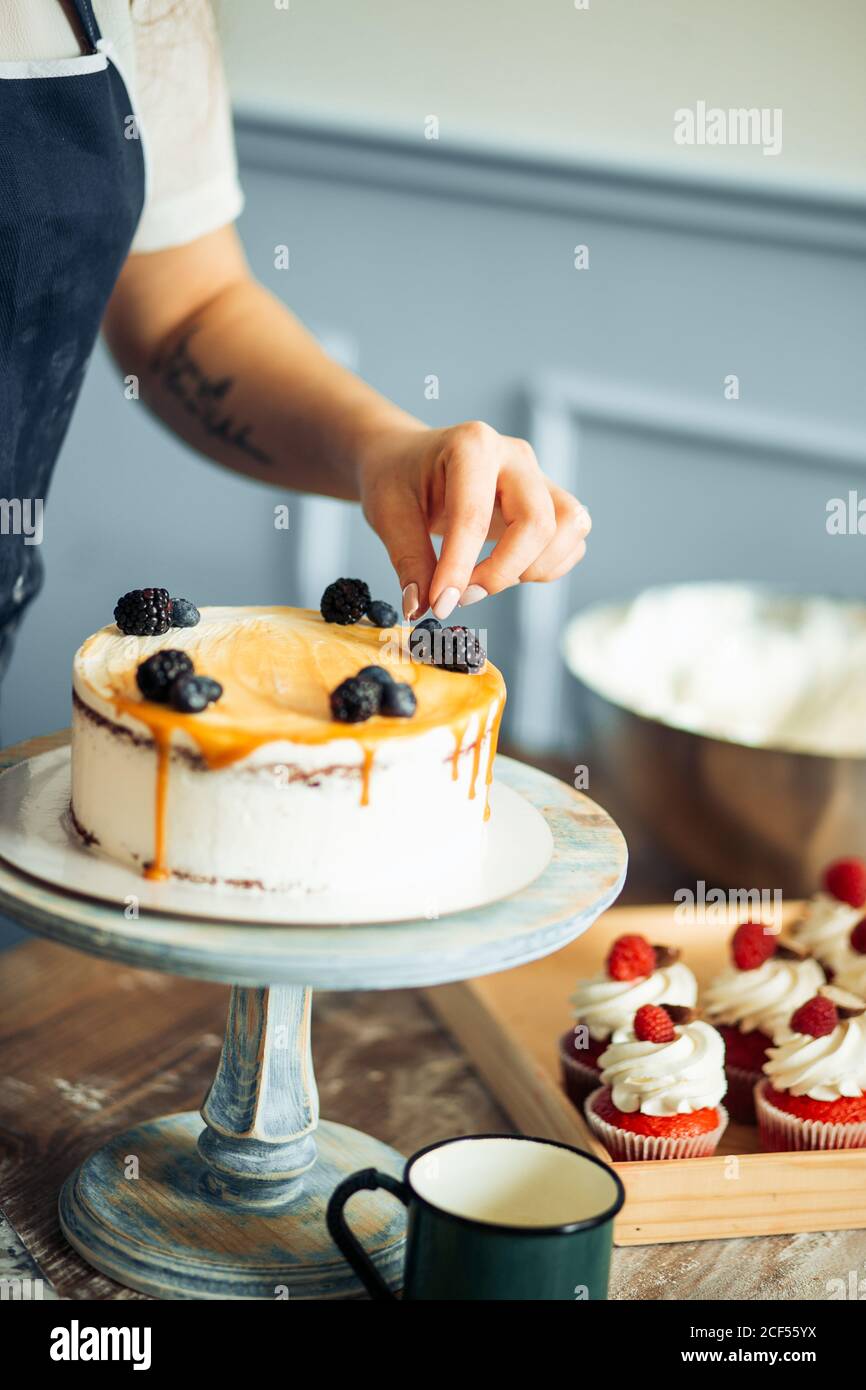 Pastry chef in the kitchen decorating a cake of chocolate,fruit,candies ...