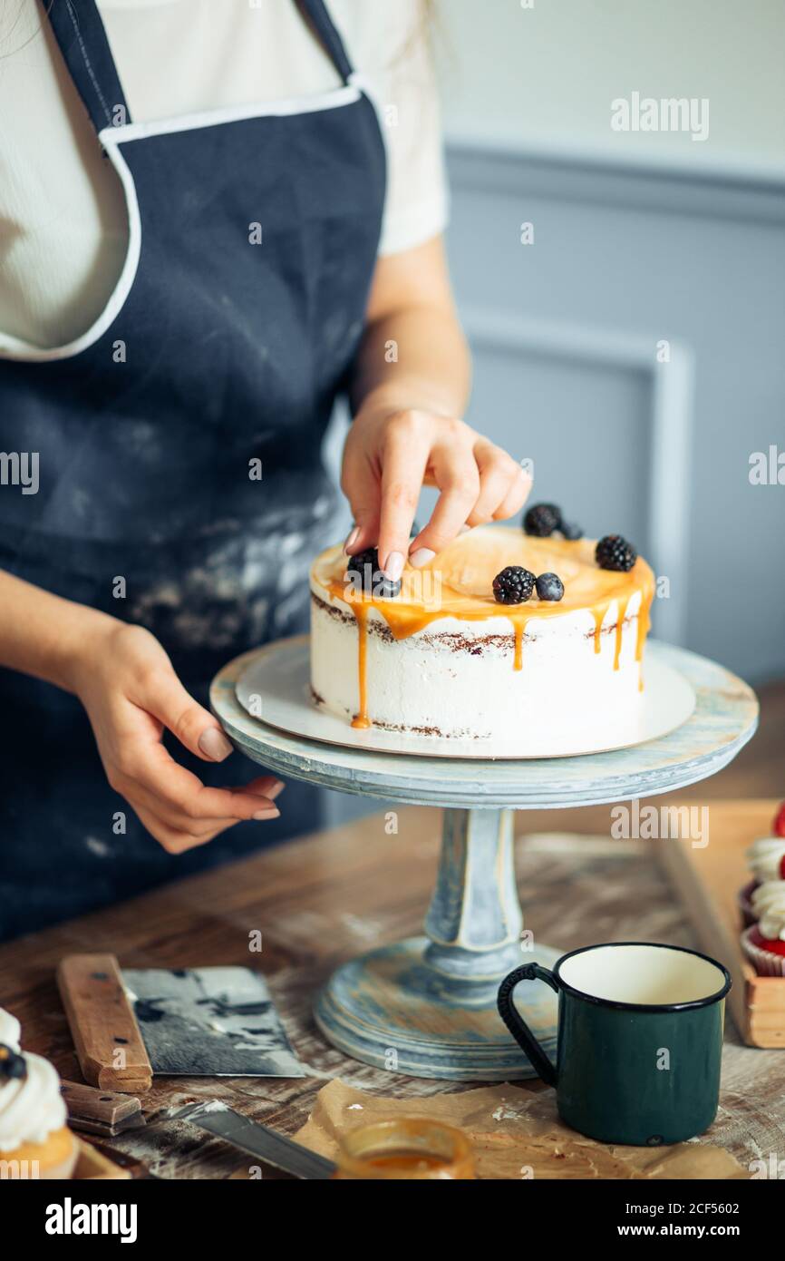 Pastry chef in the kitchen decorating a cake of chocolate,fruit,candies ...
