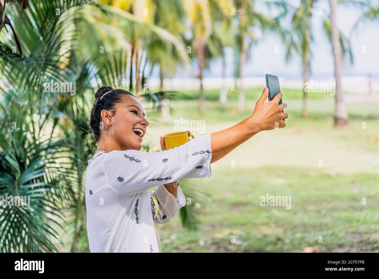 Happy Woman taking a selfie with smartphone while holding mug and ...