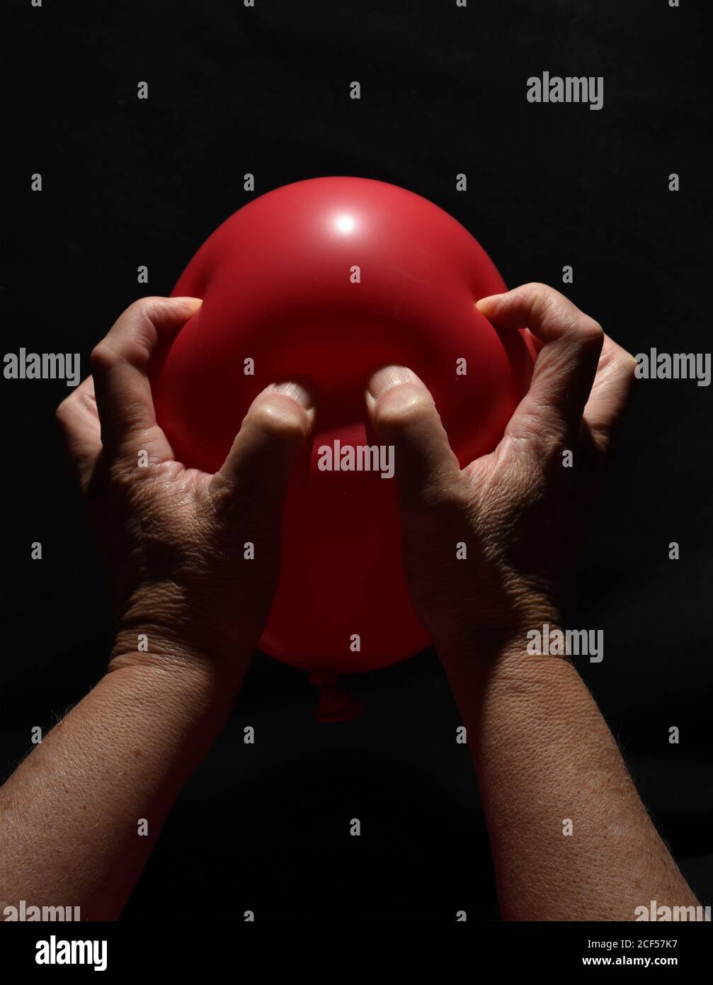 A woman’s hands aggressively squeeze an inflated red balloon against a ...